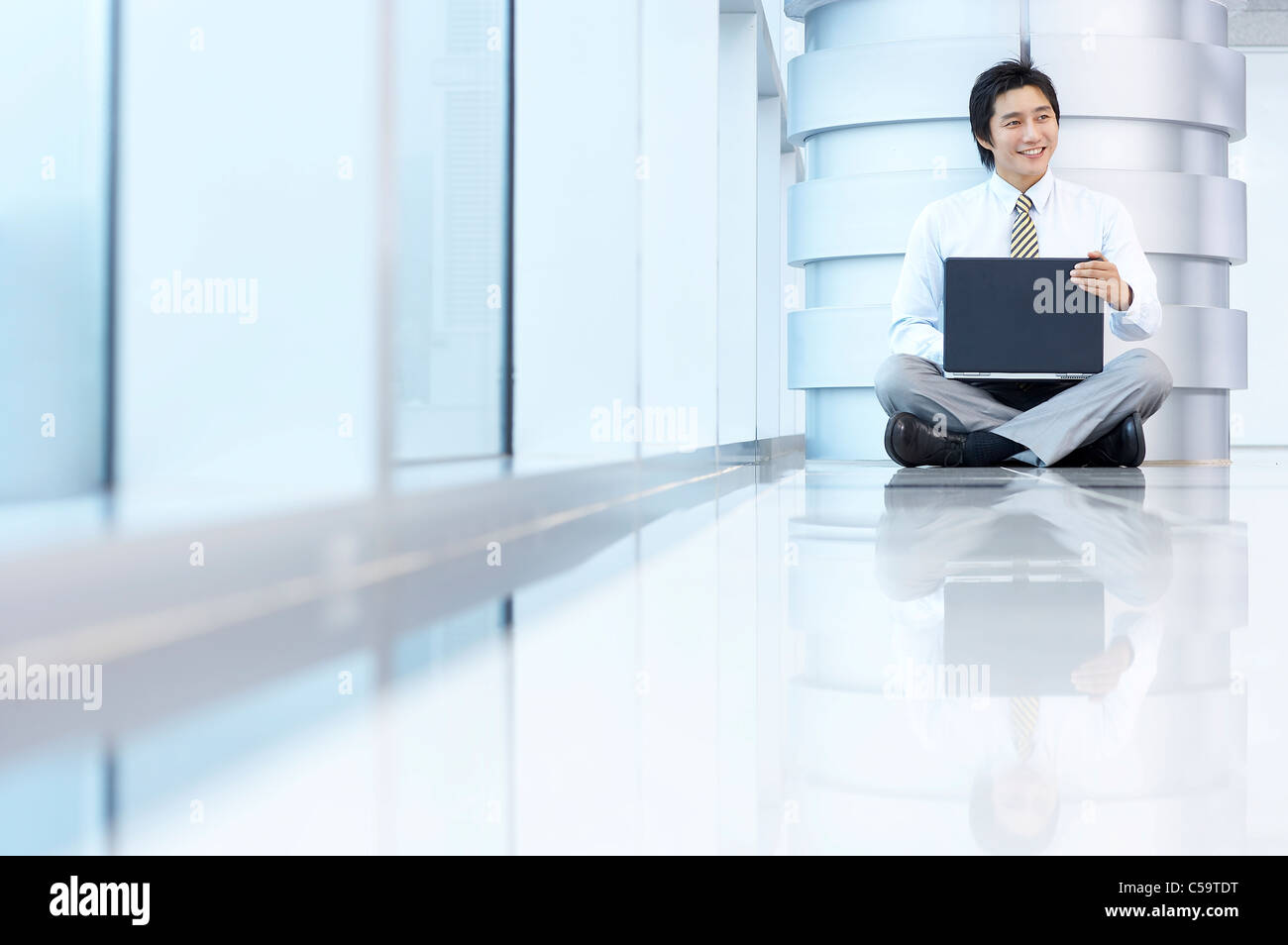 Businessman sitting by pillar, using laptop Stock Photo - Alamy