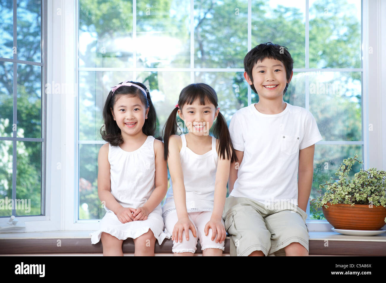Portrait of children sitting by window Stock Photo - Alamy