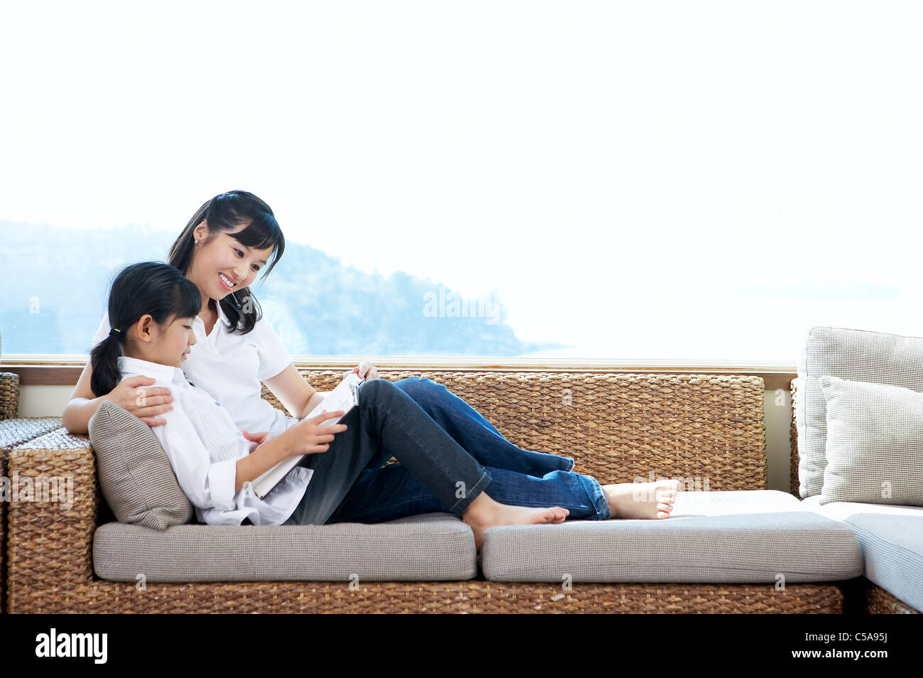 Side view of mother and daughter reading book on sofa Stock Photo - Alamy