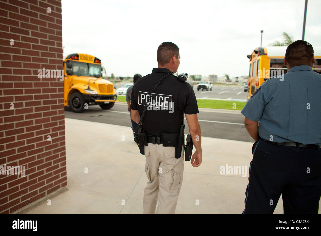 Male police officers supervises school bus loading at high school in ...