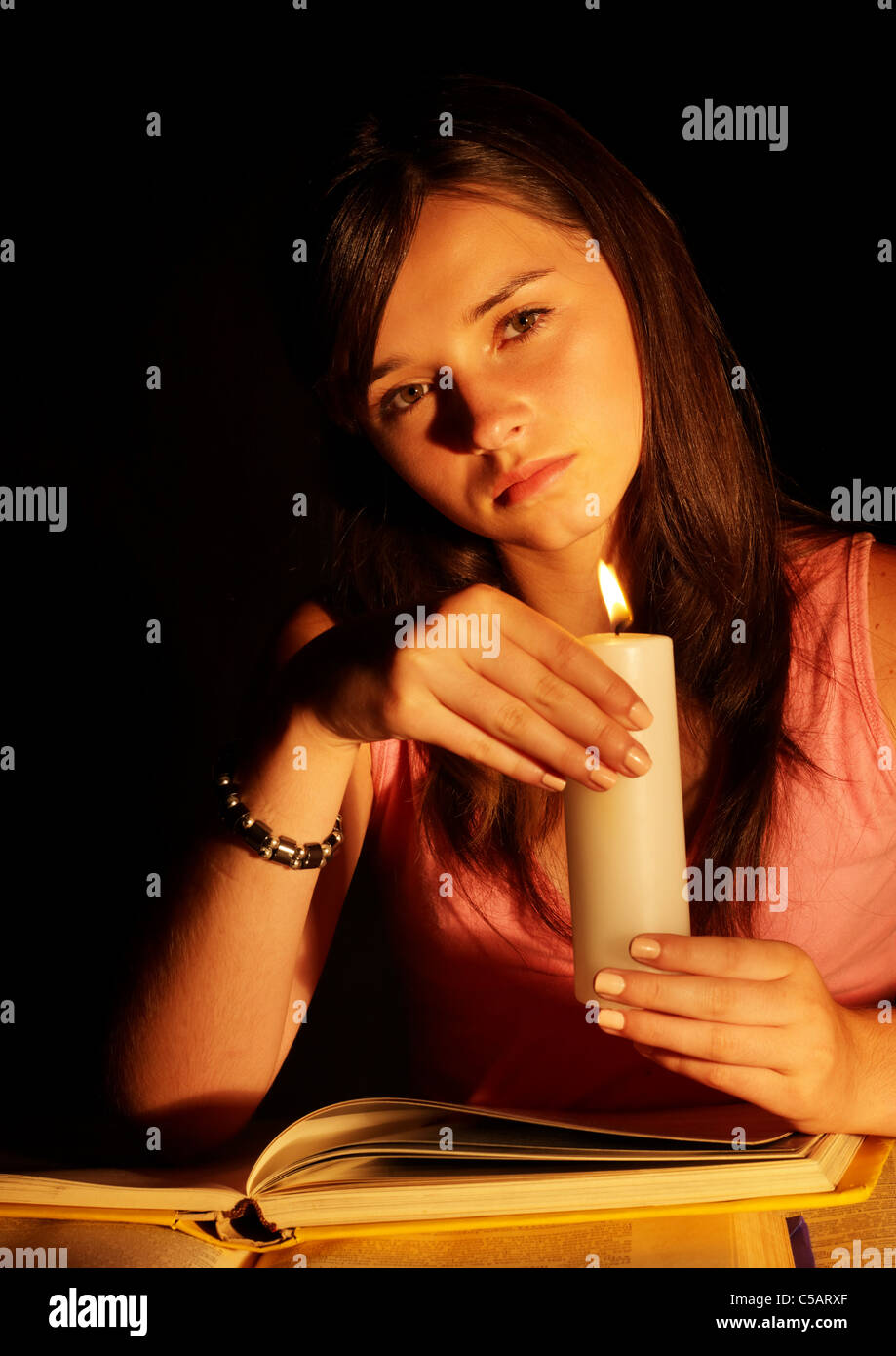 Girl reading open book on table with candle Stock Photo - Alamy
