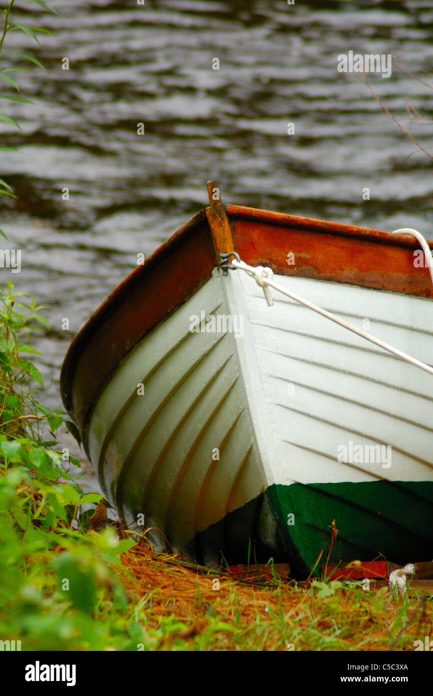a dory painted red green and white is pulled up along a riverside Stock ...
