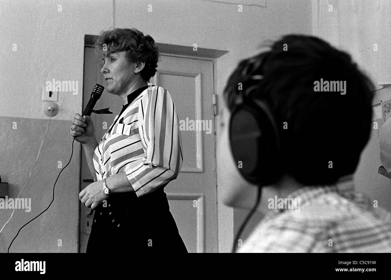 A female teacher using a microphone and earphones to aid teaching to ...