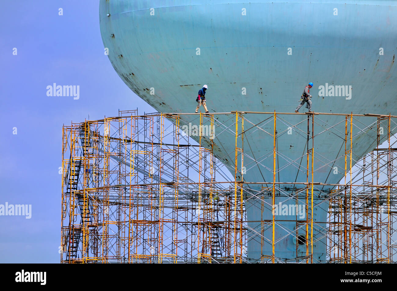 Workman walk along a catwalk atop scaffolding surrounding the water ...