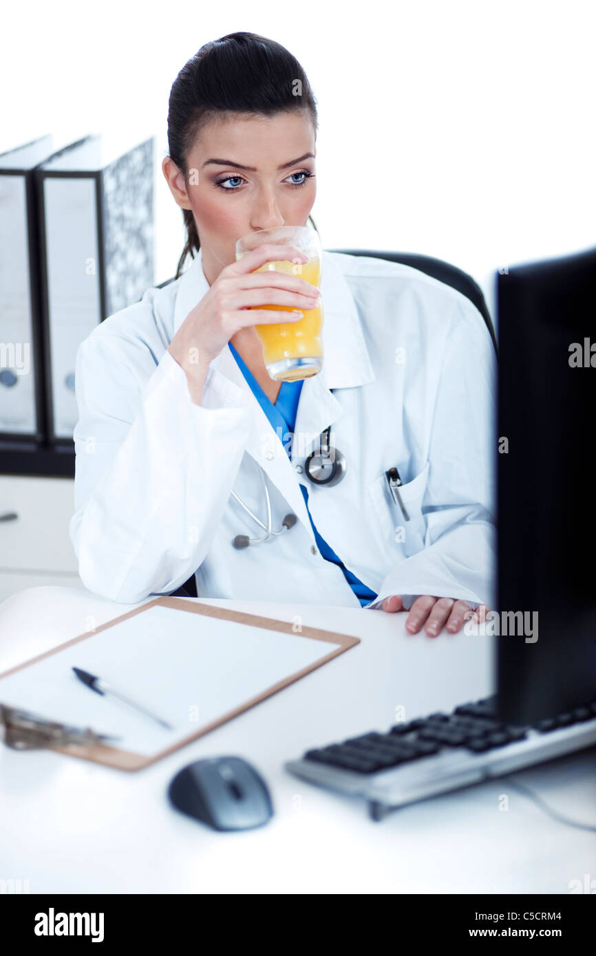 Doctor drinking a glass of juice at her workplace over white background ...