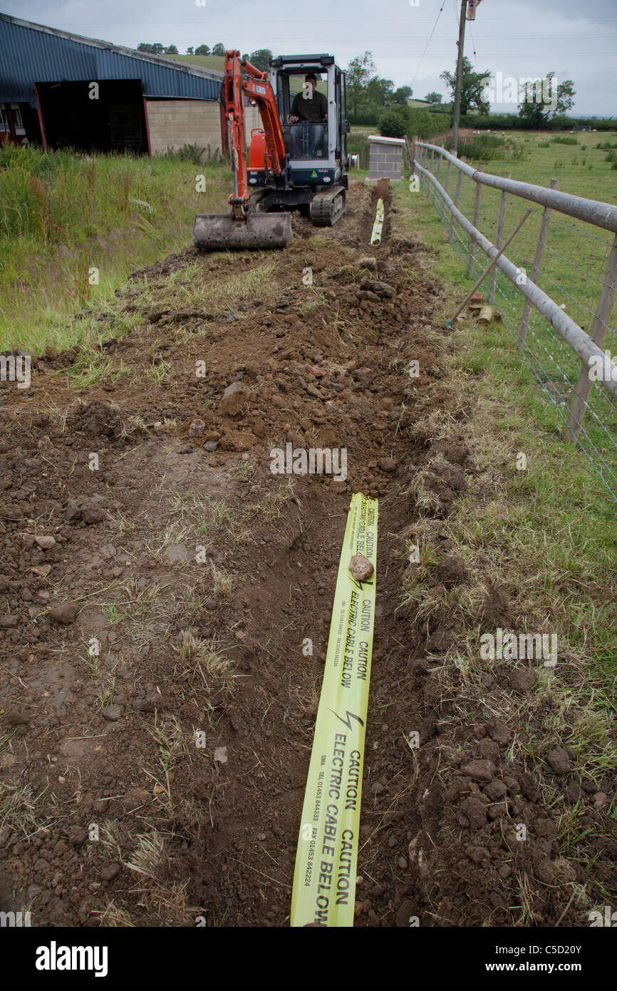 Kubota digger infilling trench with electric ducting and yellow warning ...