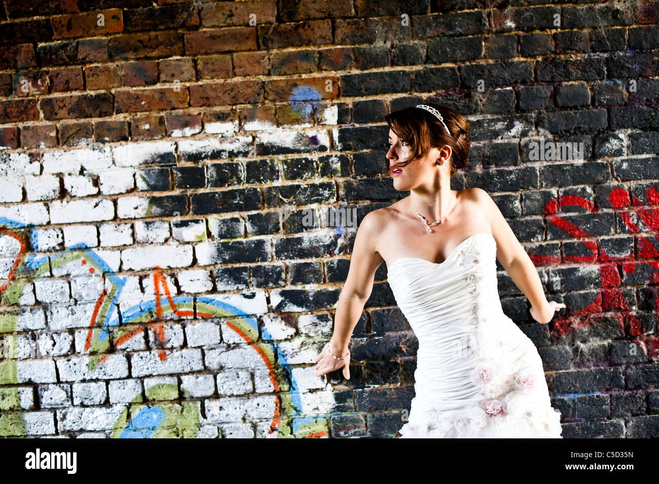 Scared Bride poses against graffiti wall in wedding dress looking away ...