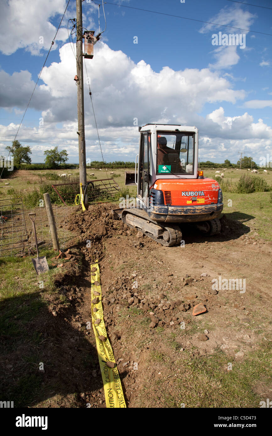 Kubota digger infilling trench with electric ducting and yellow warning ...