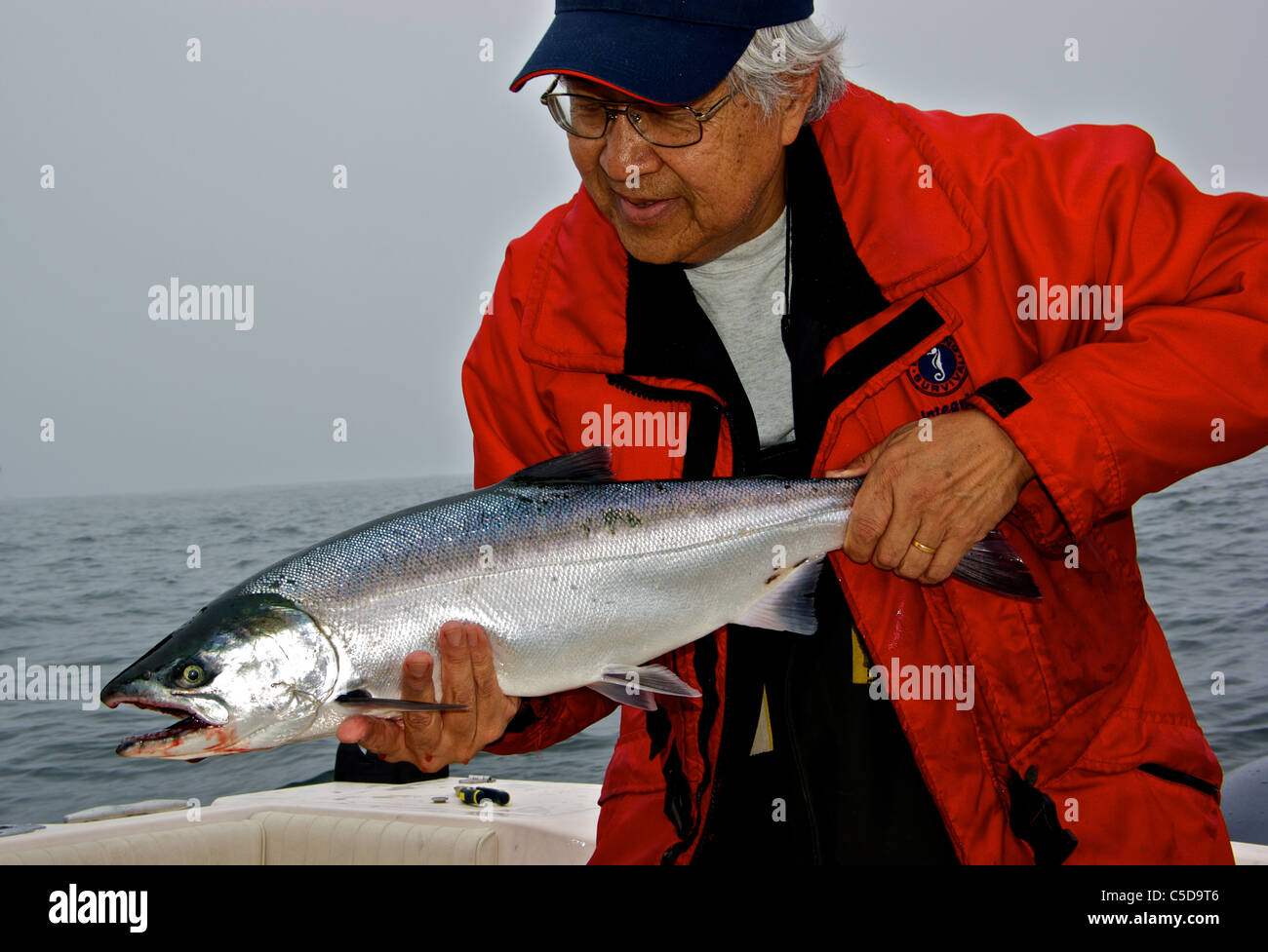 Asian male holding big adipose fin clipped hatchery coho Kyuquot Sound ...
