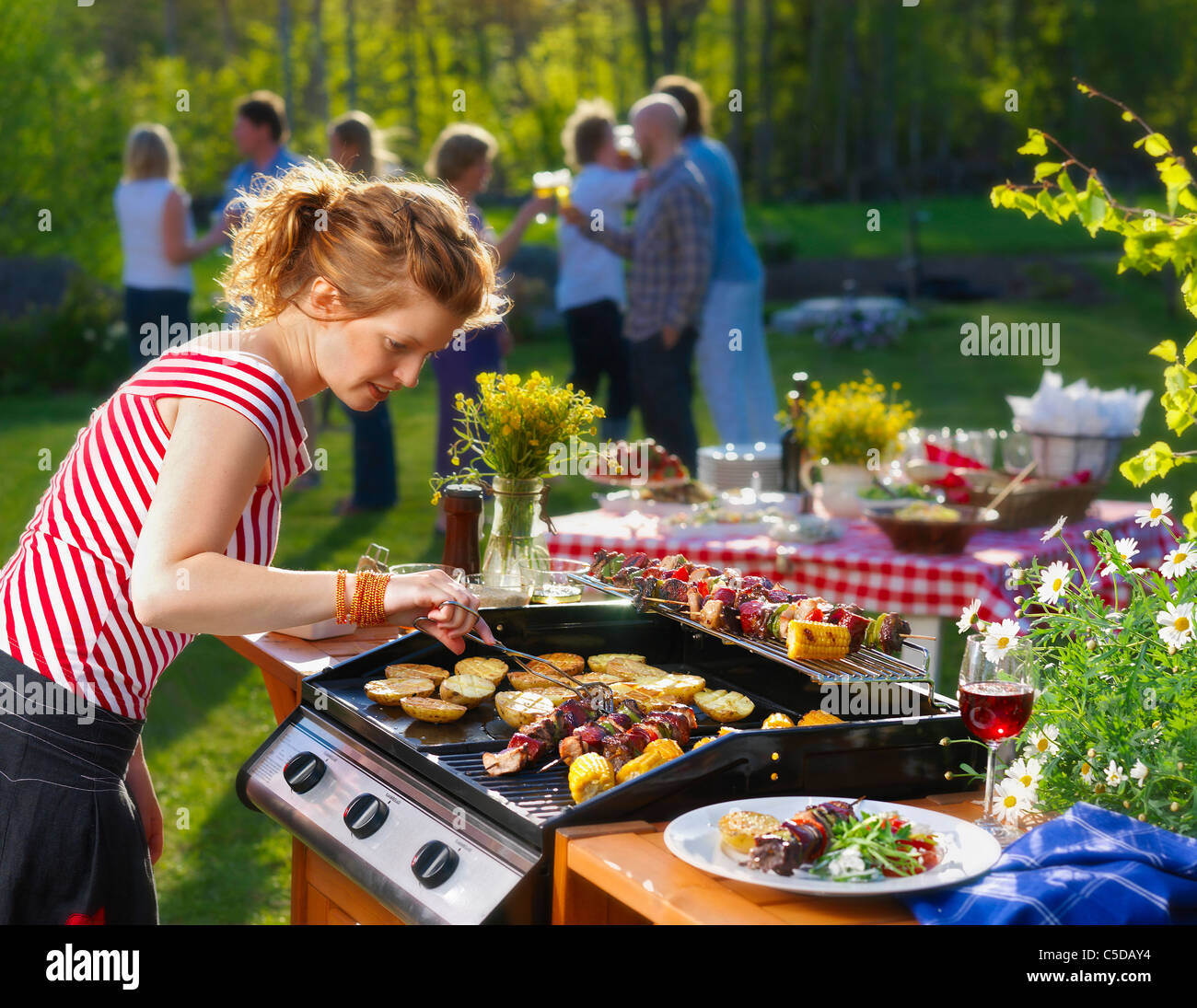 Side view of woman at barbecue grill with blurred people partying in ...