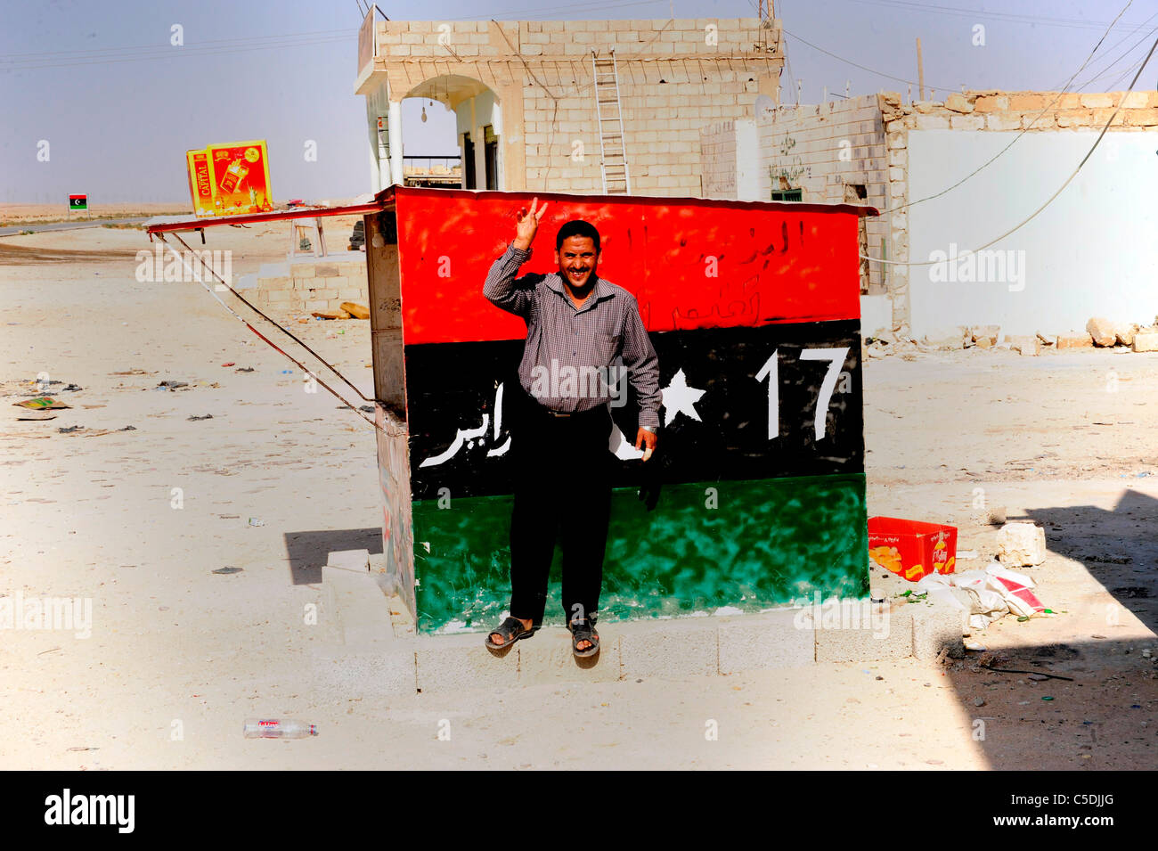a man stands infront of the new Libyan flag painted on a wall out side ...