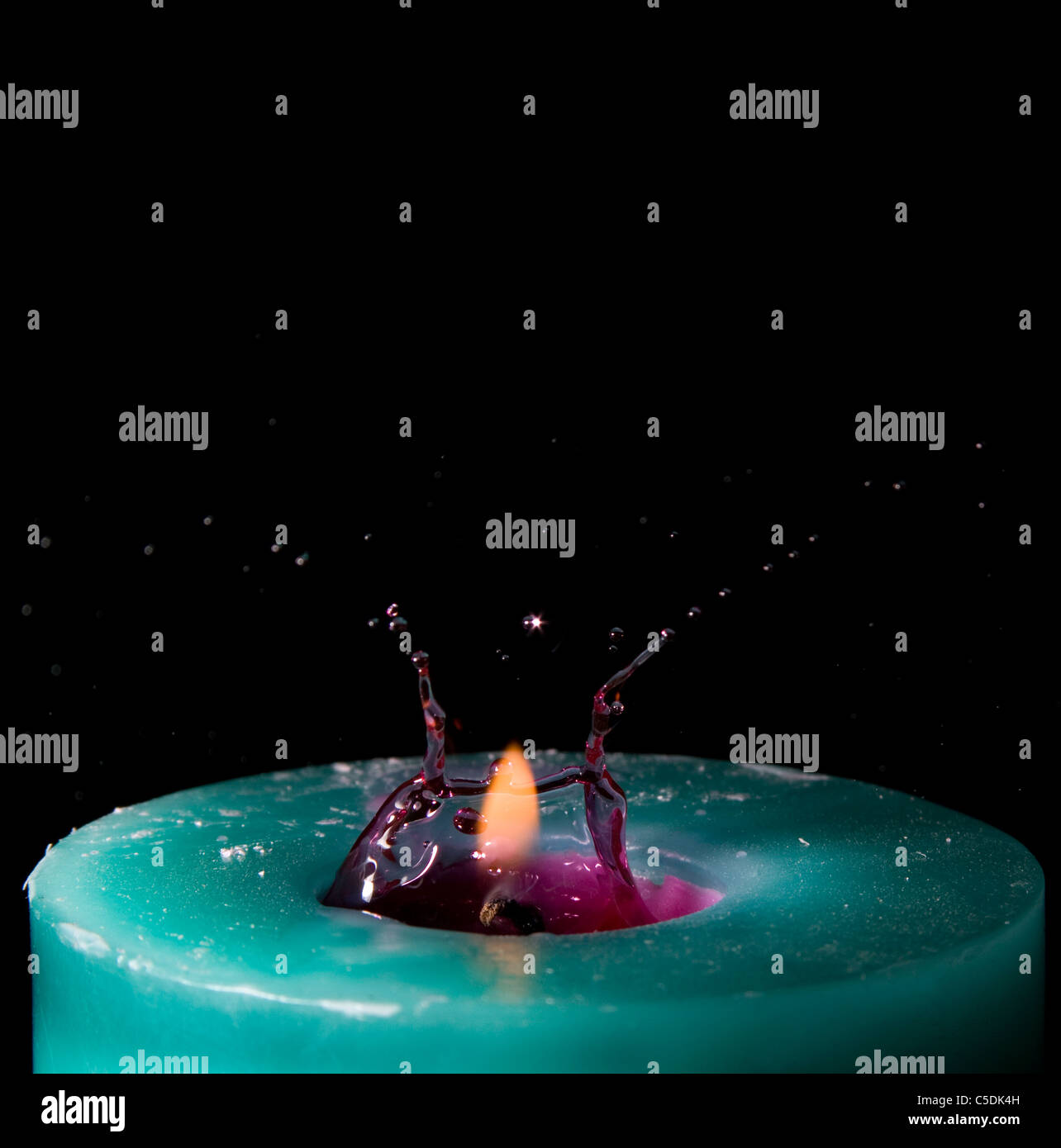 a drop of red wax dropping in to a green lit candle causing a splash of ...