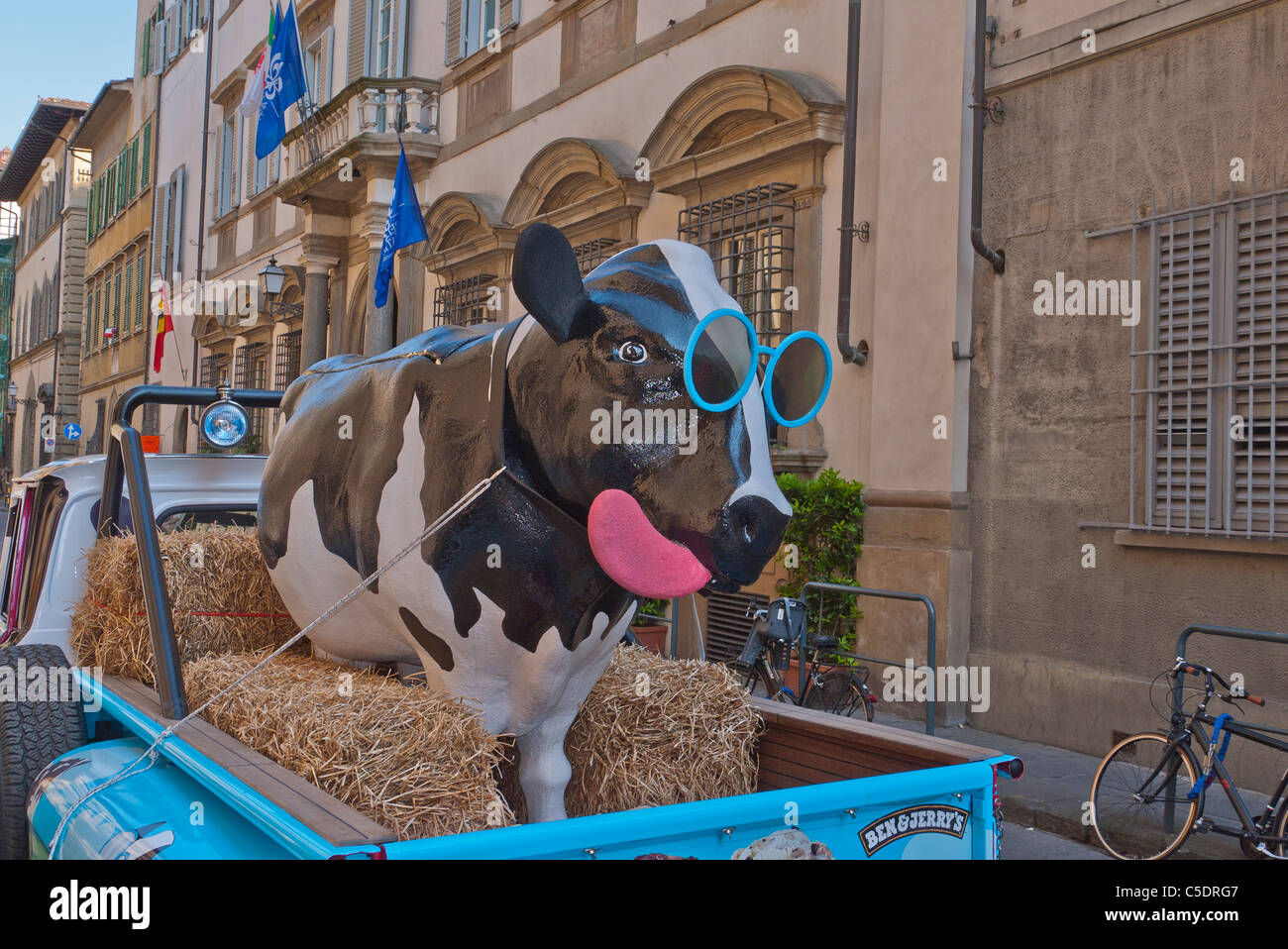 A black and white cow sculpture stands in the back of a truck with hay ...
