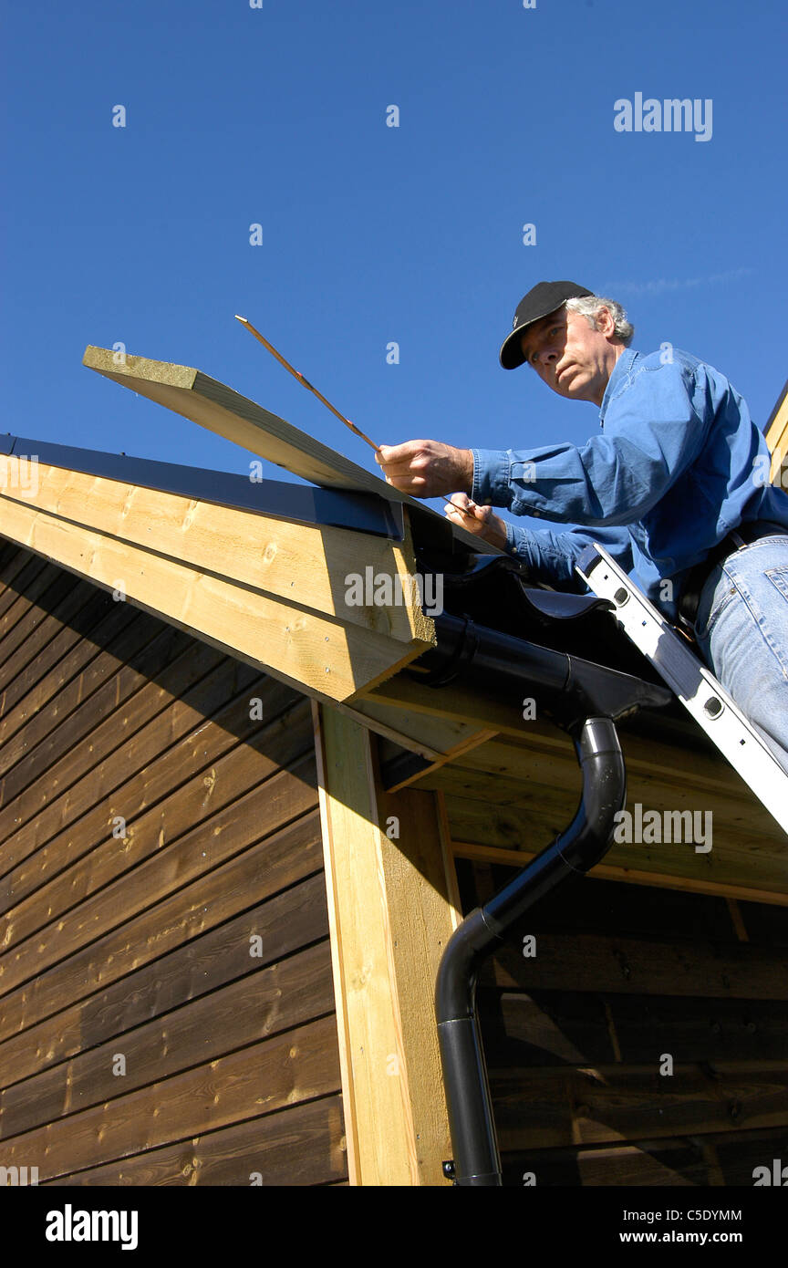 Low angle view of middle-aged man fixing house roof against blue sky ...