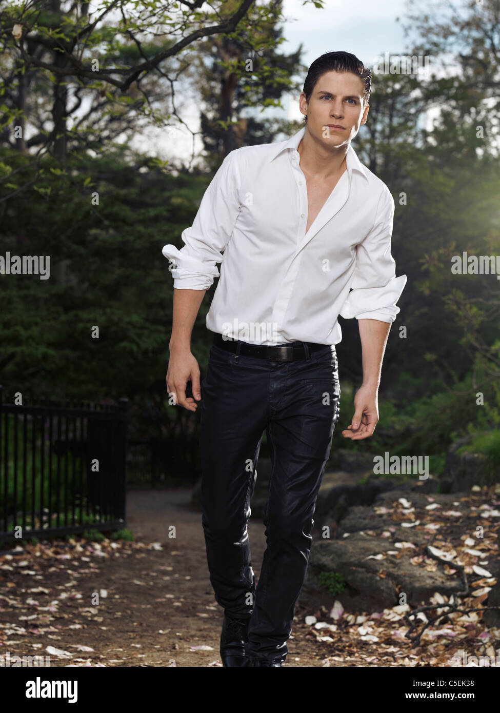 Photo of a stylish young man walking through a park in the evening ...