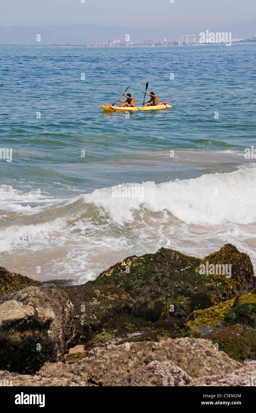 Two men kayak in Banderas Bay with the faint skyline of Puerto Vallarta ...