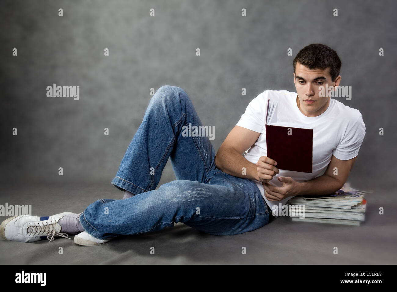A young man lying reading a book, on a gray background Stock Photo - Alamy