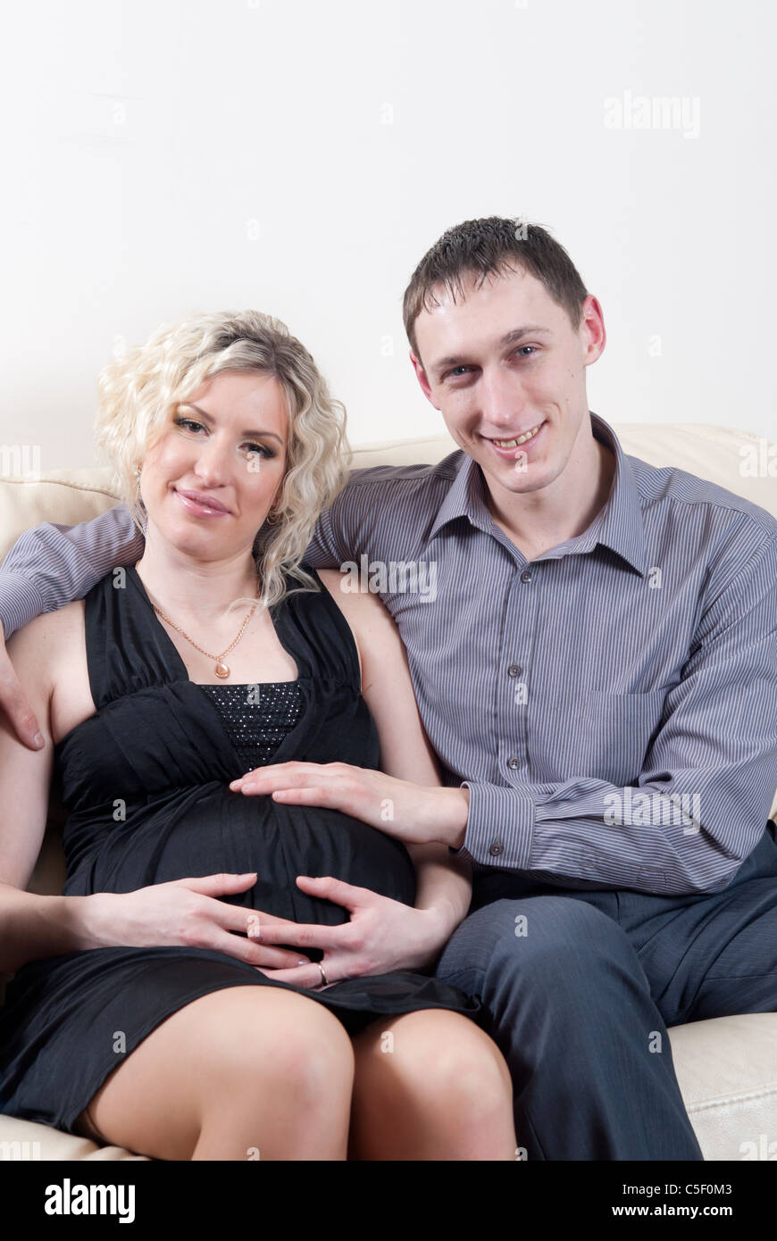 Happy pregnant couple sat on sofa Stock Photo - Alamy
