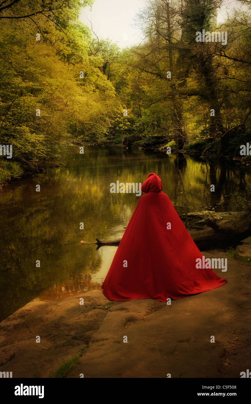 Mysterious person in red cape in the forest by the lake Stock Photo - Alamy