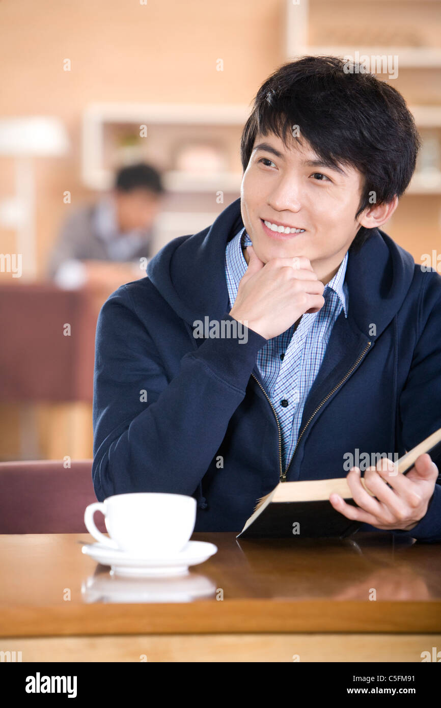 Young man taking a break from reading a book at a coffee shop Stock ...