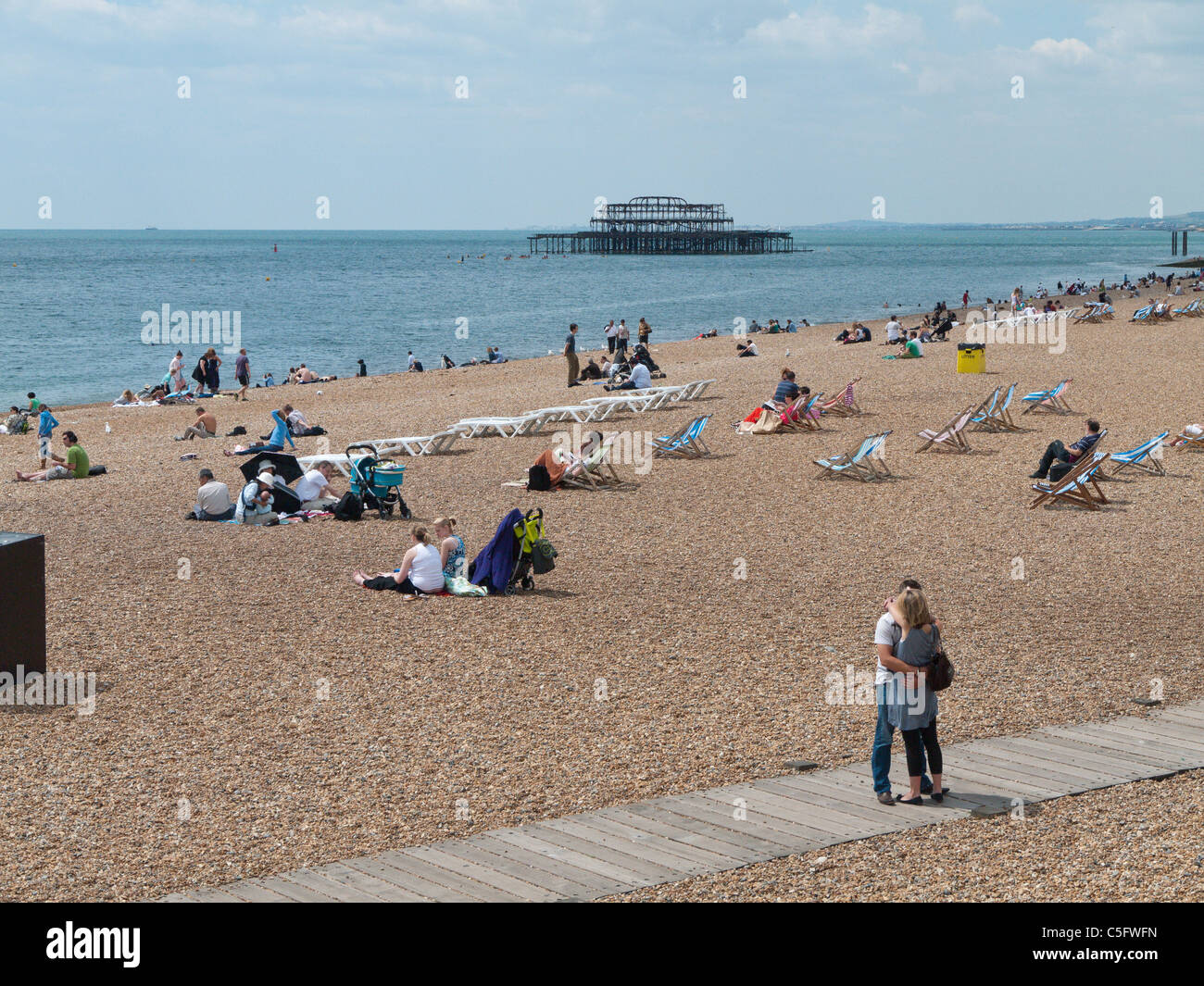 Brighton beach scene with sunbathers on deck chairs and the ruined west ...