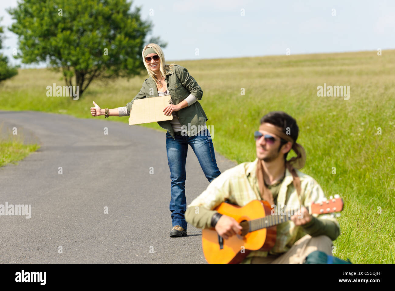 Hitch-hike young couple backpack tramping on asphalt road play guitar ...