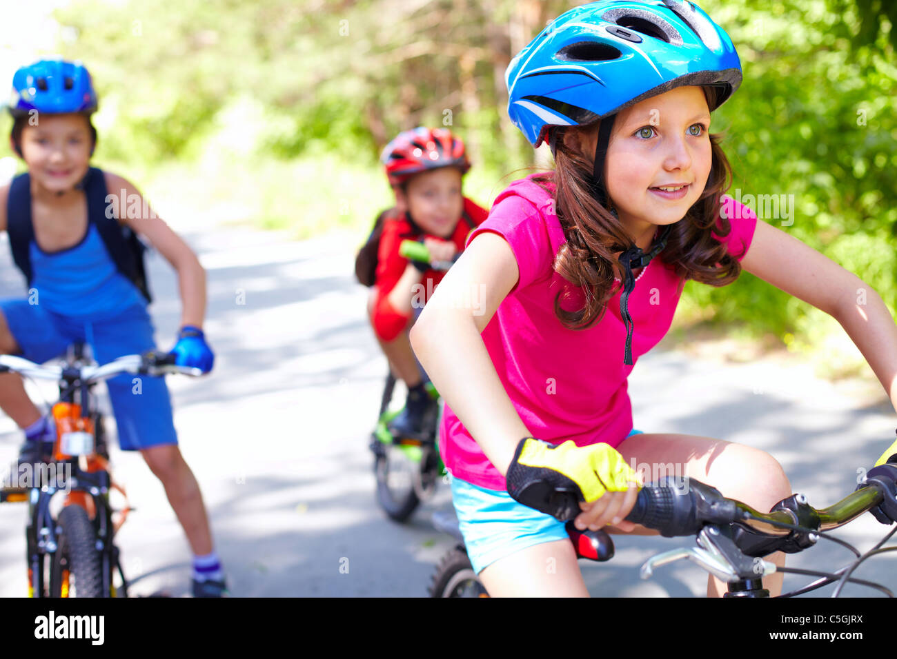 A little girl riding her bike with two friends behind Stock Photo - Alamy