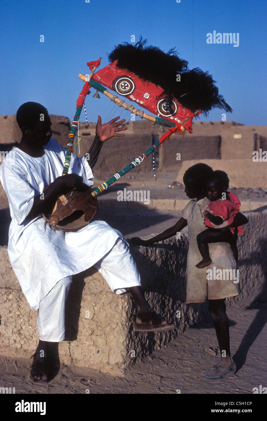Man playing a traditional musical instrument with a child watching ...
