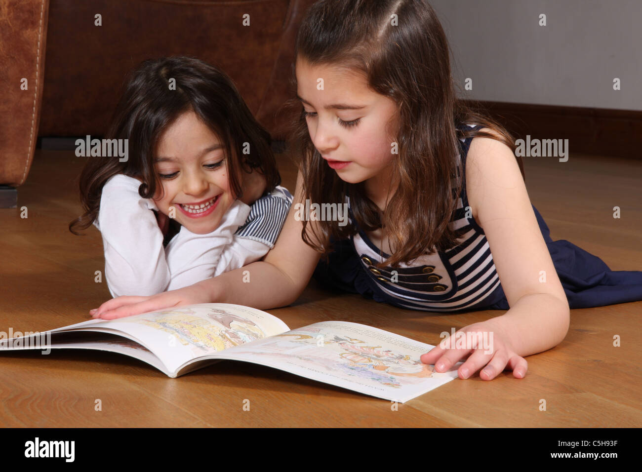 Two sisters reading a picture book Stock Photo - Alamy