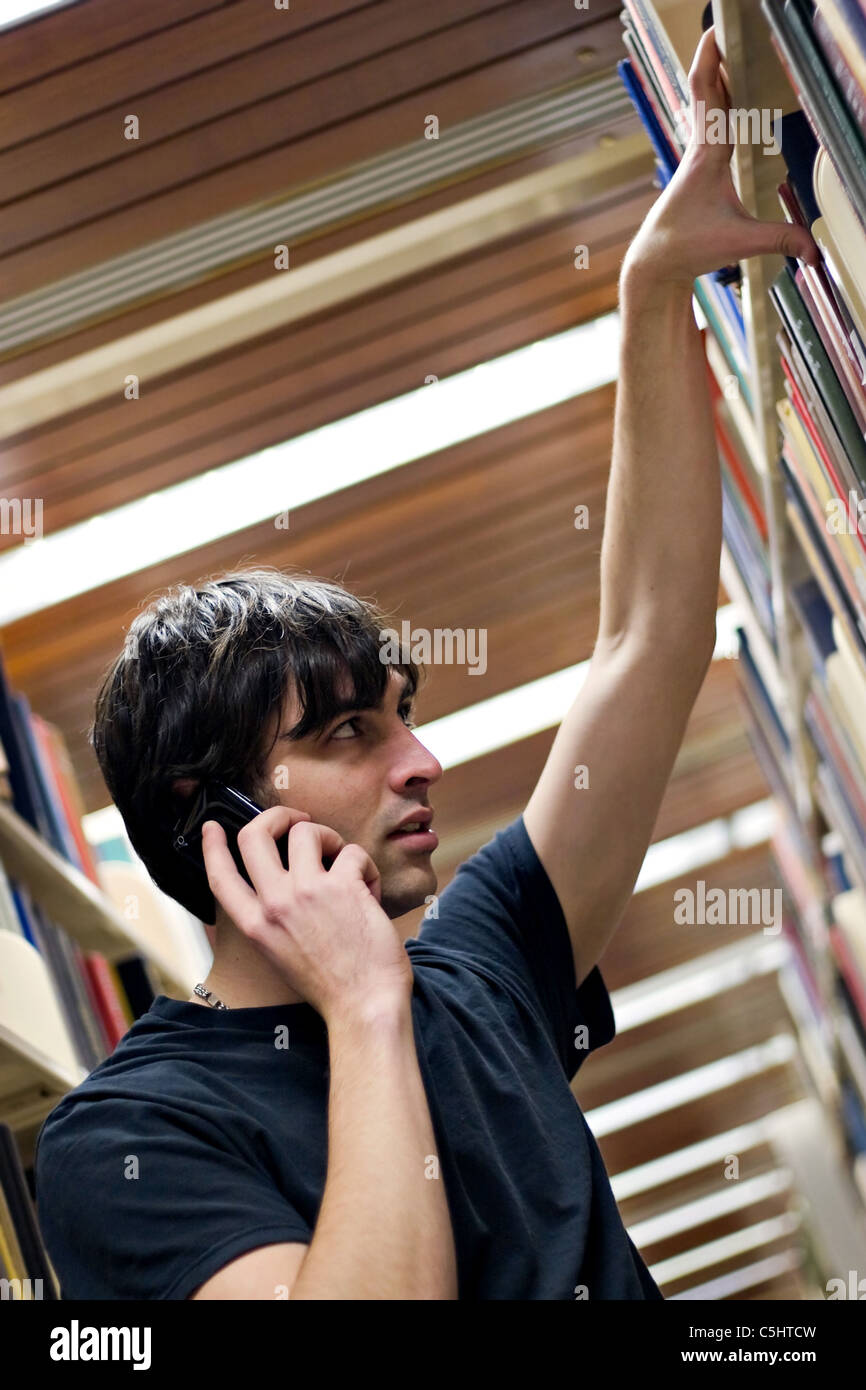 A young man searching for a book or topic at the library while doing ...