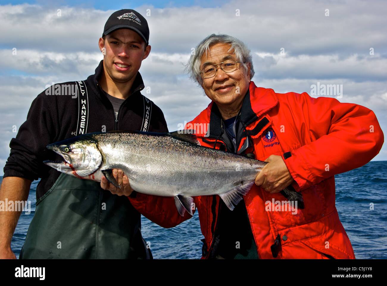 Sport fishing guide Asian charter guest holding catch of Chinook salmon ...