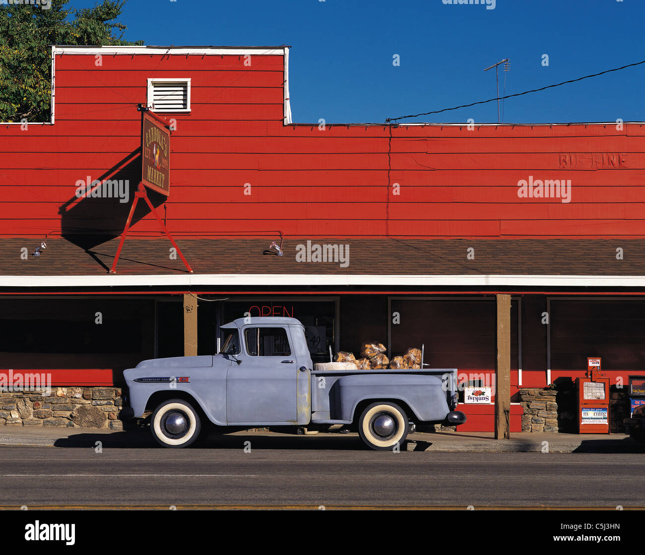 Old-style grey pick-up truck parked in front of red-painted store ...