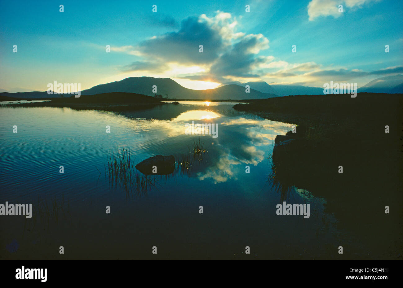 Dramatic sunset behind rolling hills reflected in still water, Rannoch ...