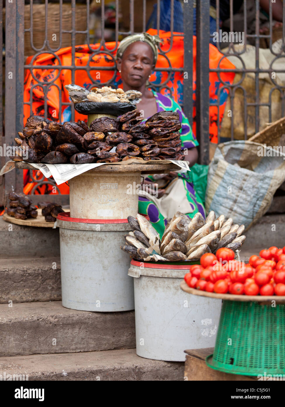 African vendor resting on market stall selling smoked fish and fresh ...