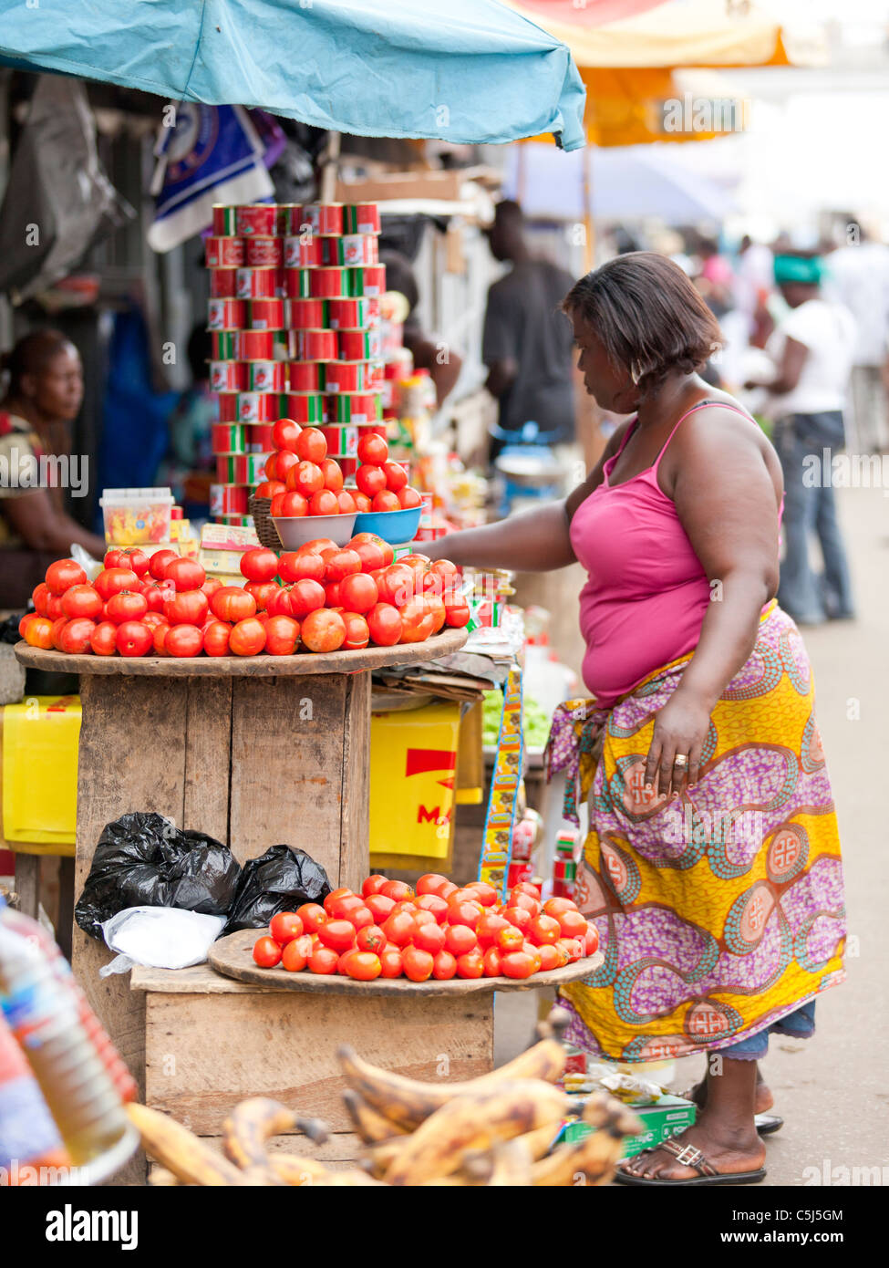 African woman selecting fresh tomatoes from market stall, Kaneshie ...