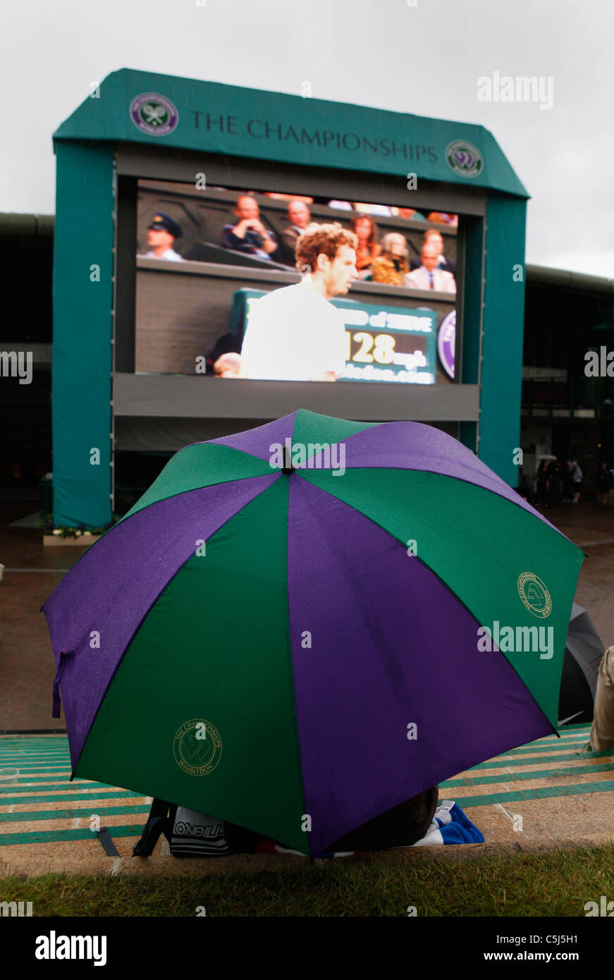 Spectator under an umbrella watching play on the big screen at ...