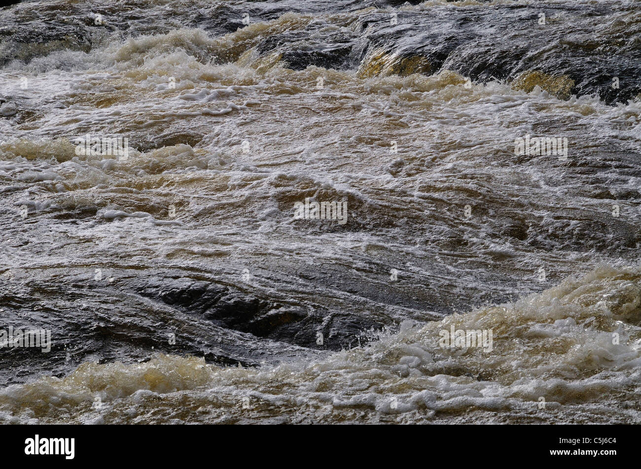 Close-up on fast-running water with brown floodwater and white rapids ...