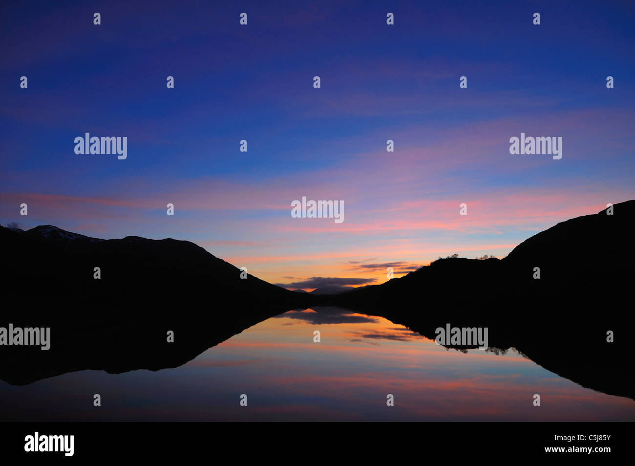Pink and deep blue sunset with silhouetted black hills reflected in the ...