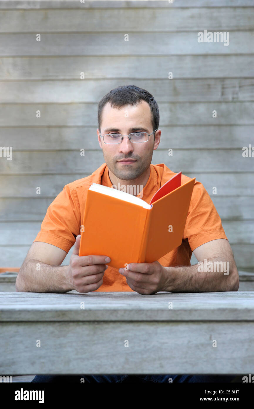 young man in orange shirt reading an orange book outdoors Stock Photo ...
