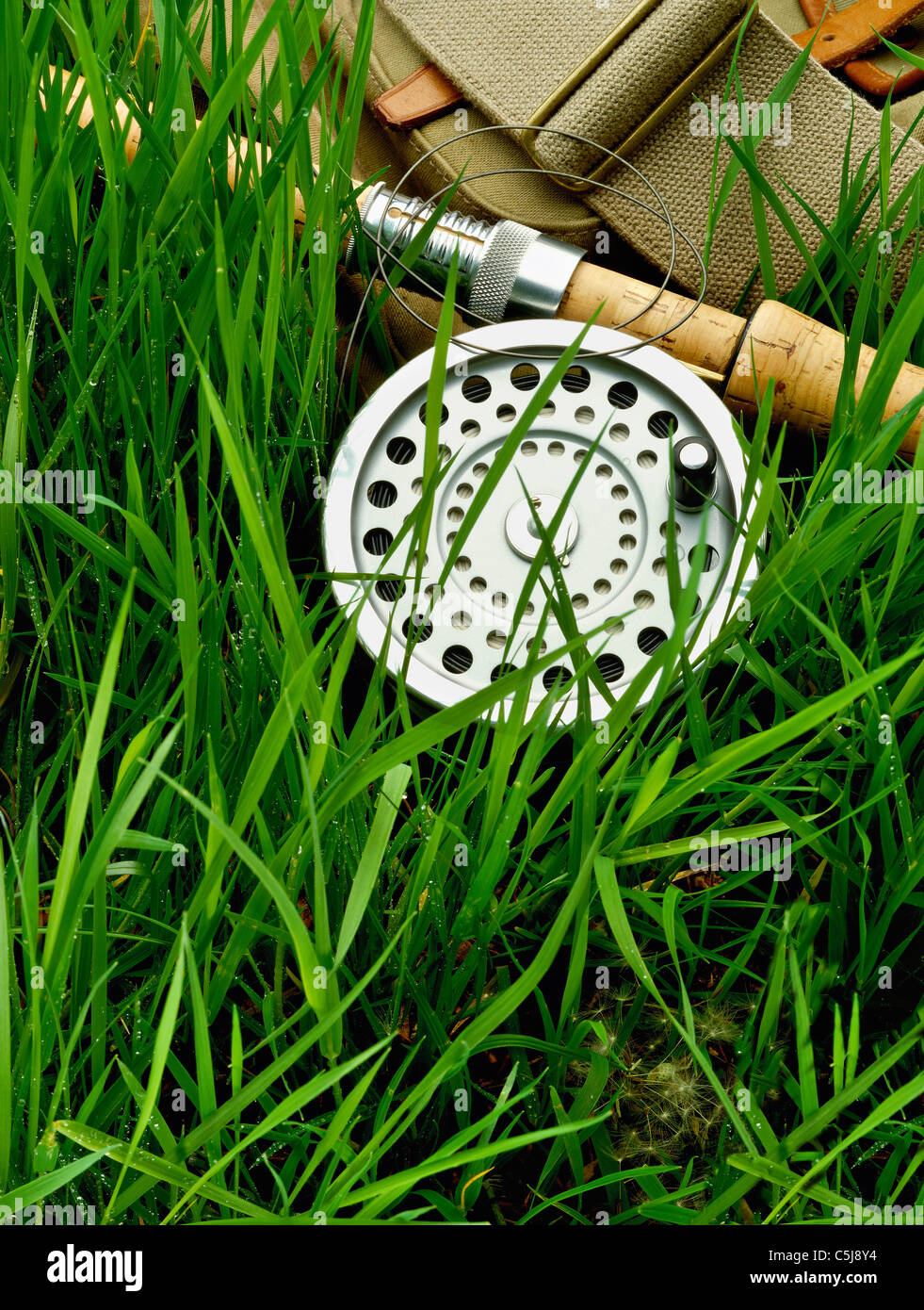Still-life of canvas fishingbag, rod, reel and line lying in lush green ...