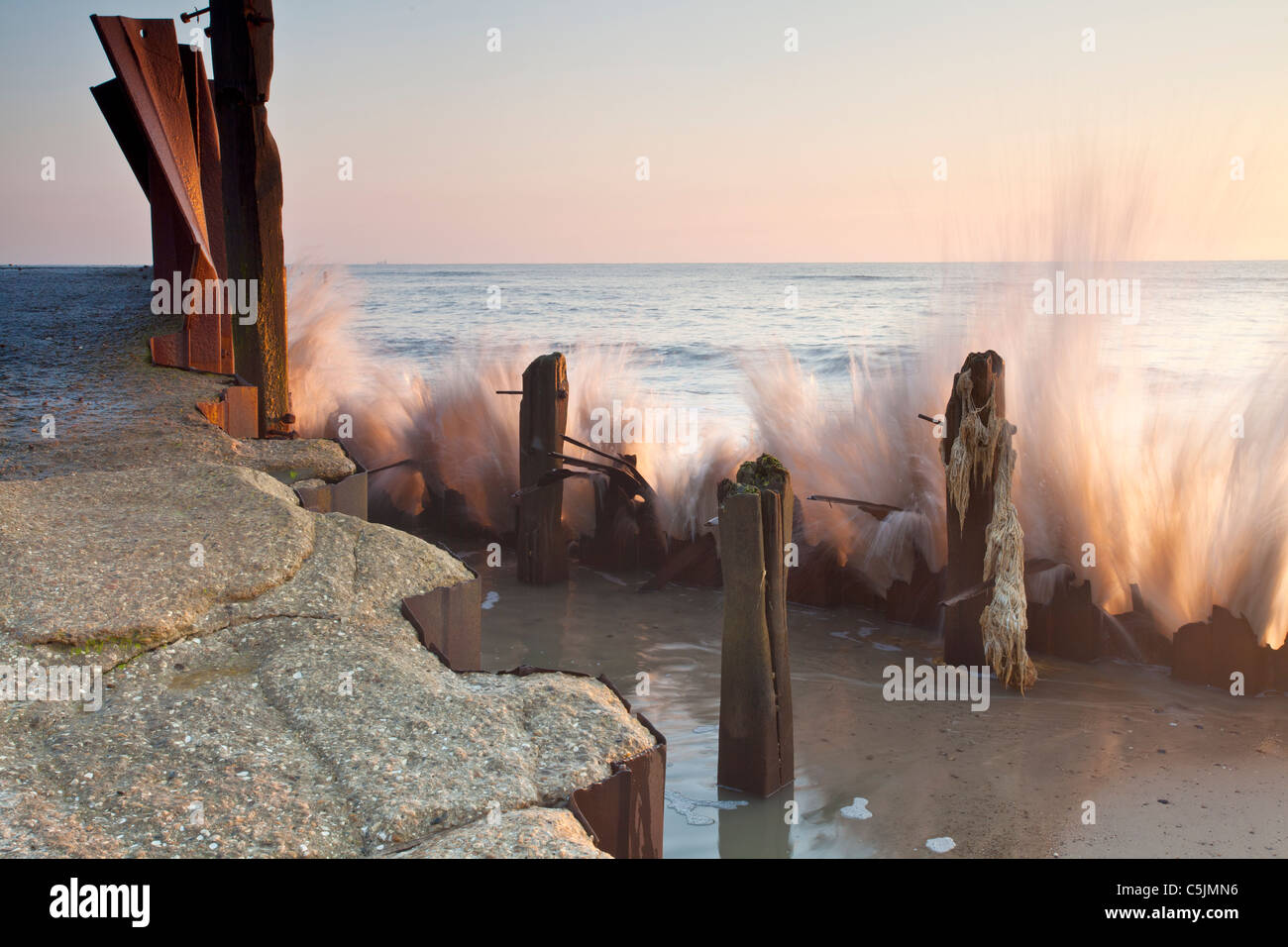Powerful waves crash against the derelict wooden and metal sea defences ...