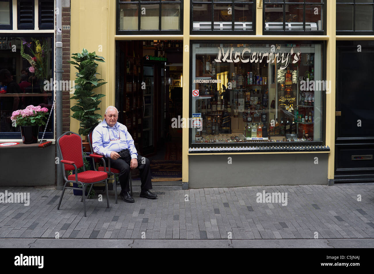 Proprietor of a small shop selling alcoholic drink sitting outside his ...