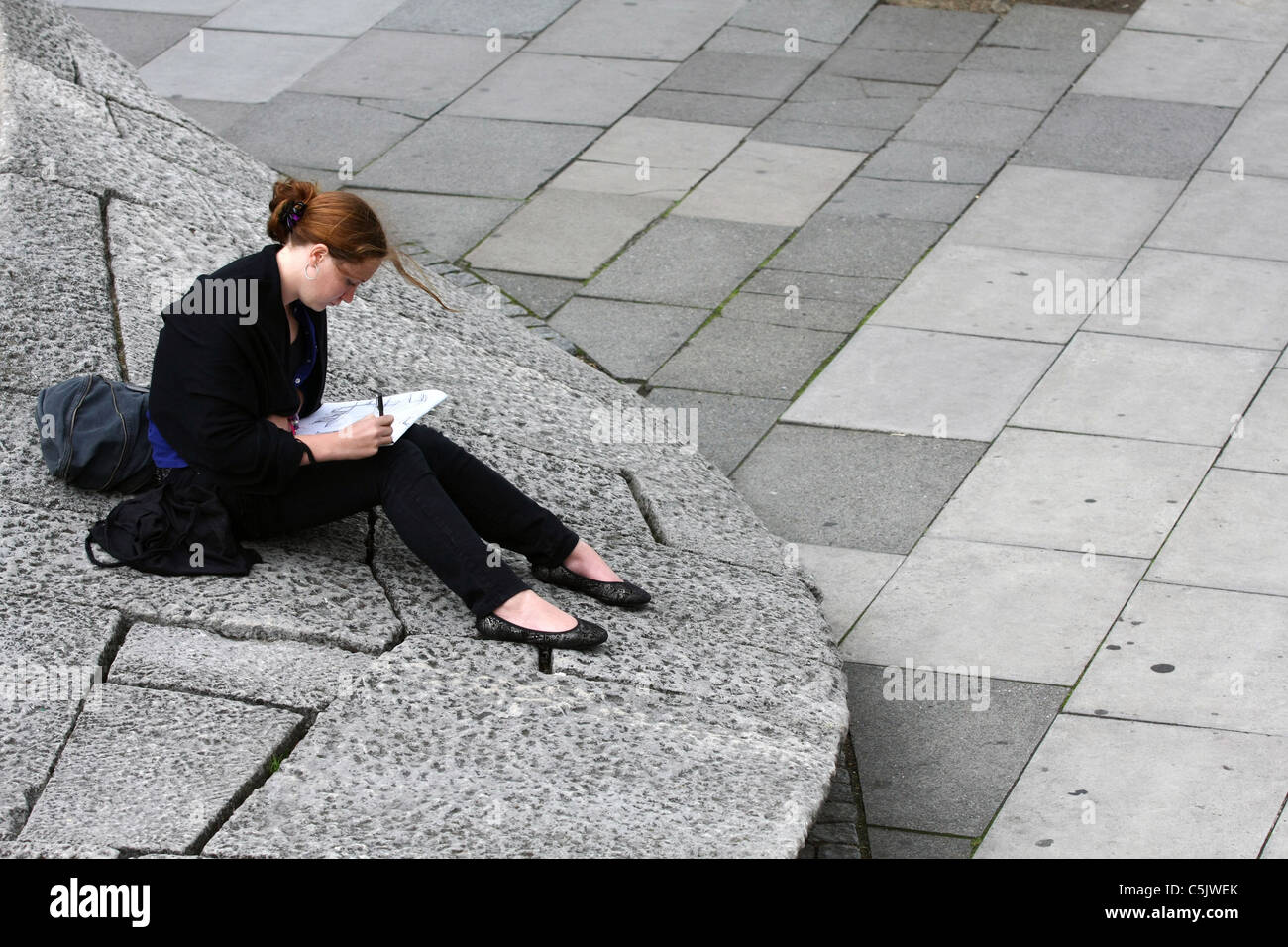 A young girl drawing while sitting on the ground on the embankment of ...