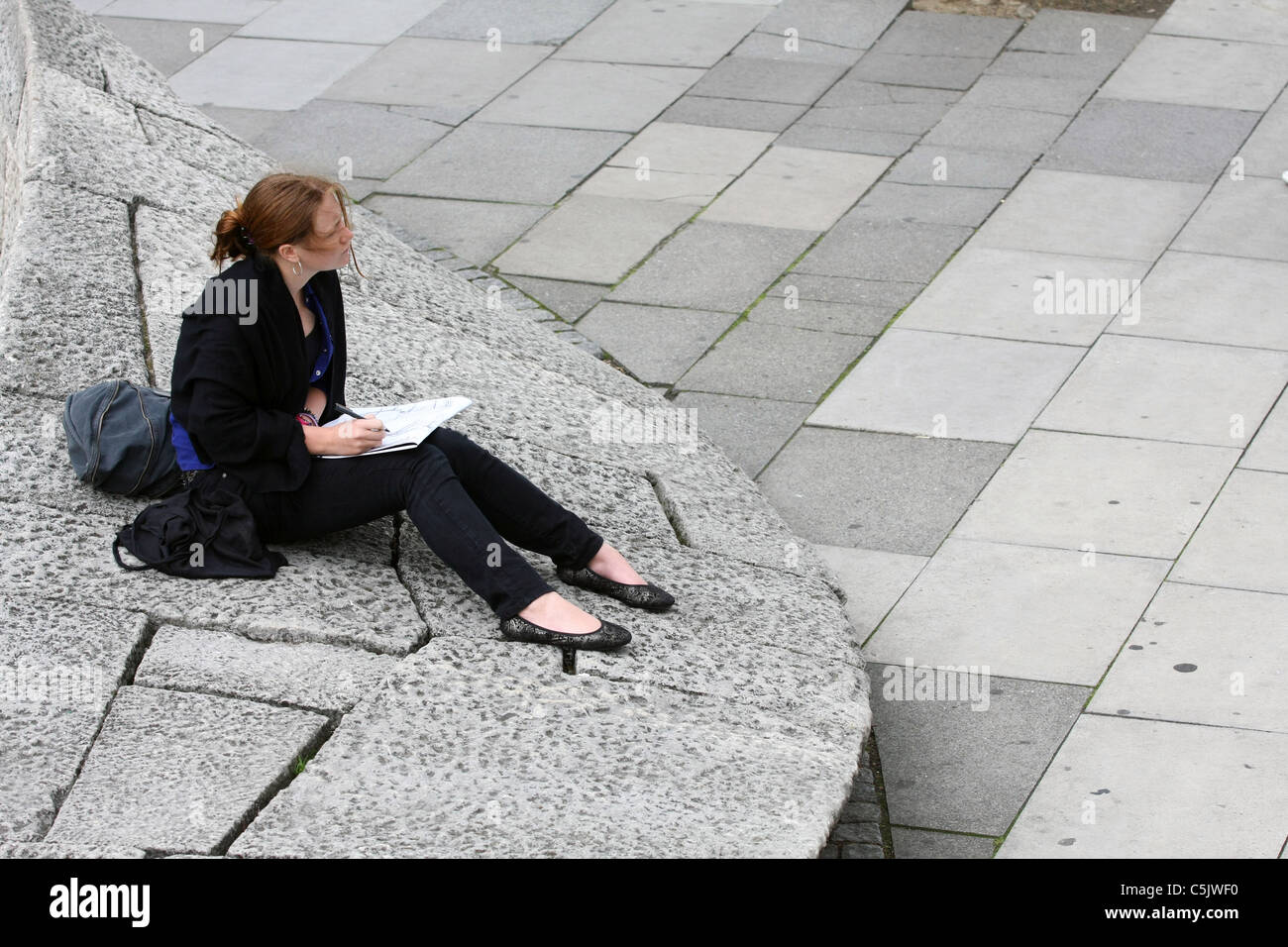A young girl drawing while sitting on the ground on the embankment of ...