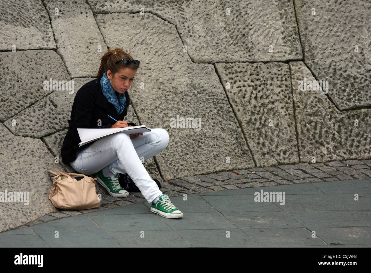A young girl drawing while sitting on the ground on the embankment of ...