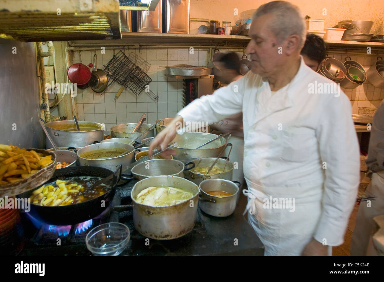 Old cook making French fries in small restaurant kitchen with food in ...