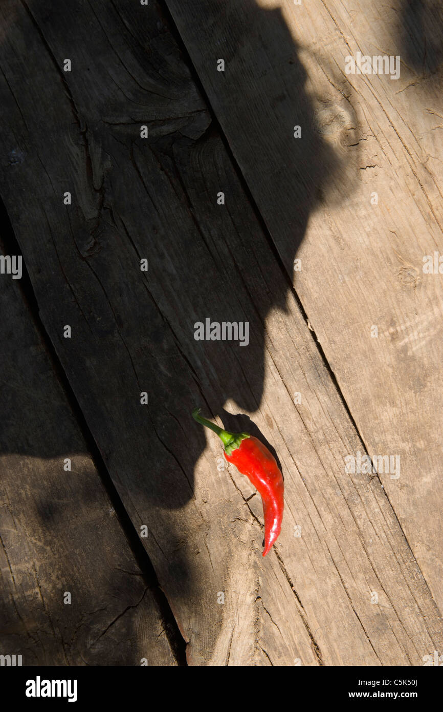 Male face shadow cast over wooden table as if holding a red pepper with ...