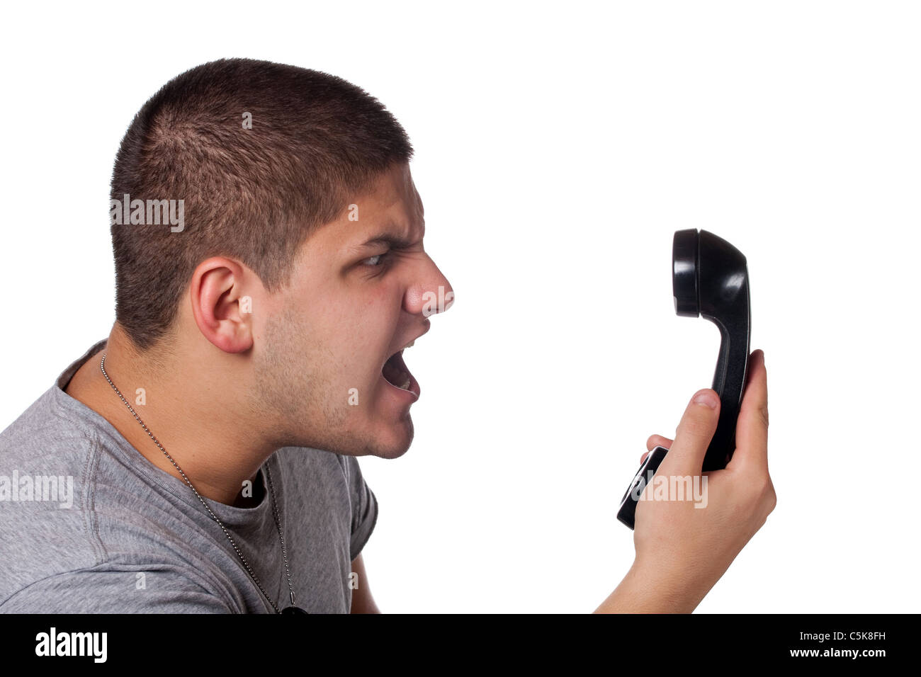 An angry and irritated young man yells into the telephone receiver over ...