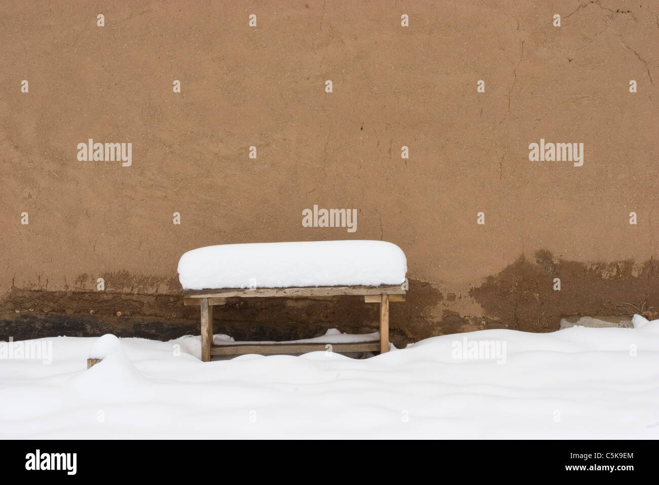 Snow-covered bench near adobe wall Stock Photo - Alamy