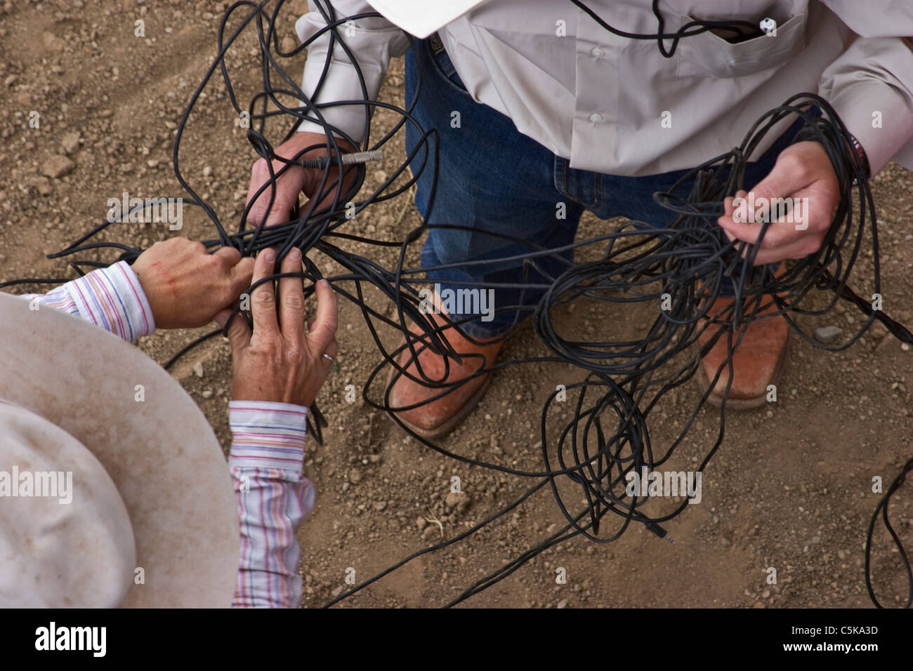 Two cowboys try to uncoil a mess of wire to set up a timing light at ...
